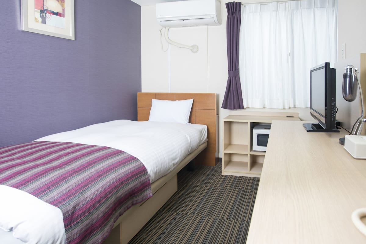 Quarto de hotel com cama, escrivaninha, televisão e ar condicionado.