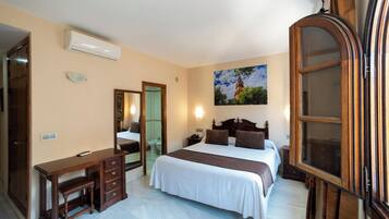 Quarto de hotel com cama, escrivaninha, guarda-roupa, espelho e um quadro na parede.