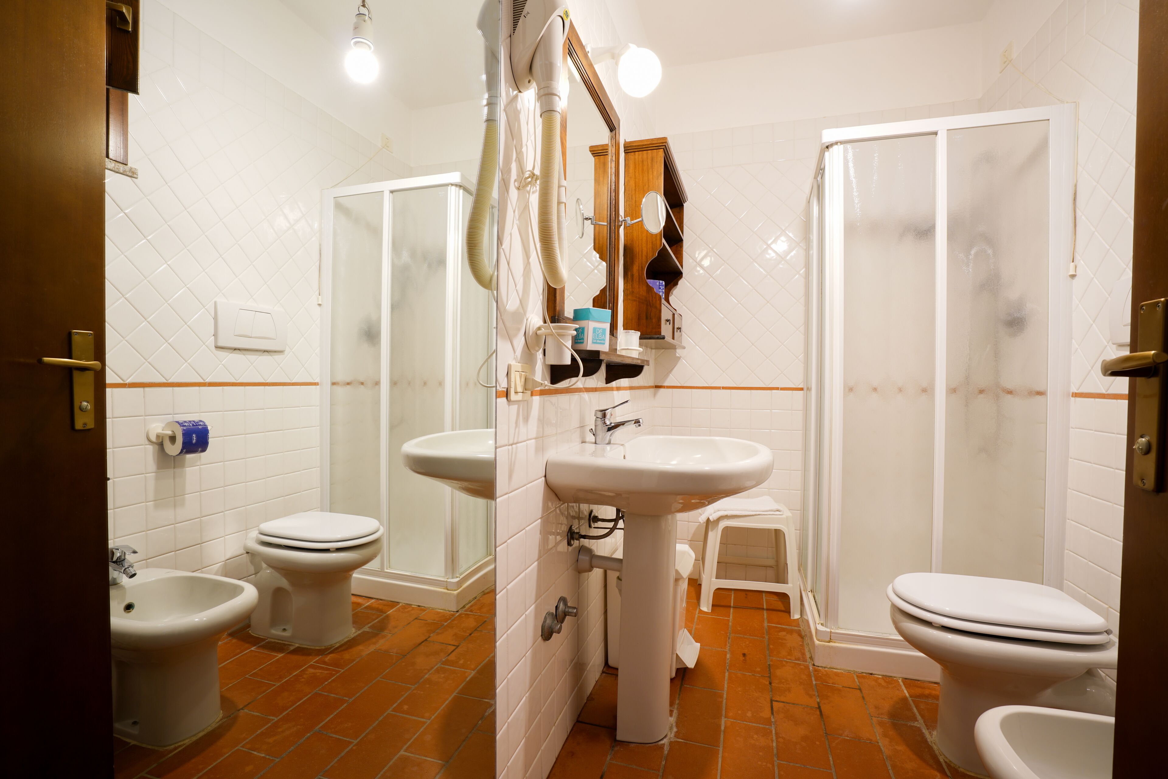 Uma casa de banho com bidé, duas sanitas, uma pia, um espelho e cabine de duche.