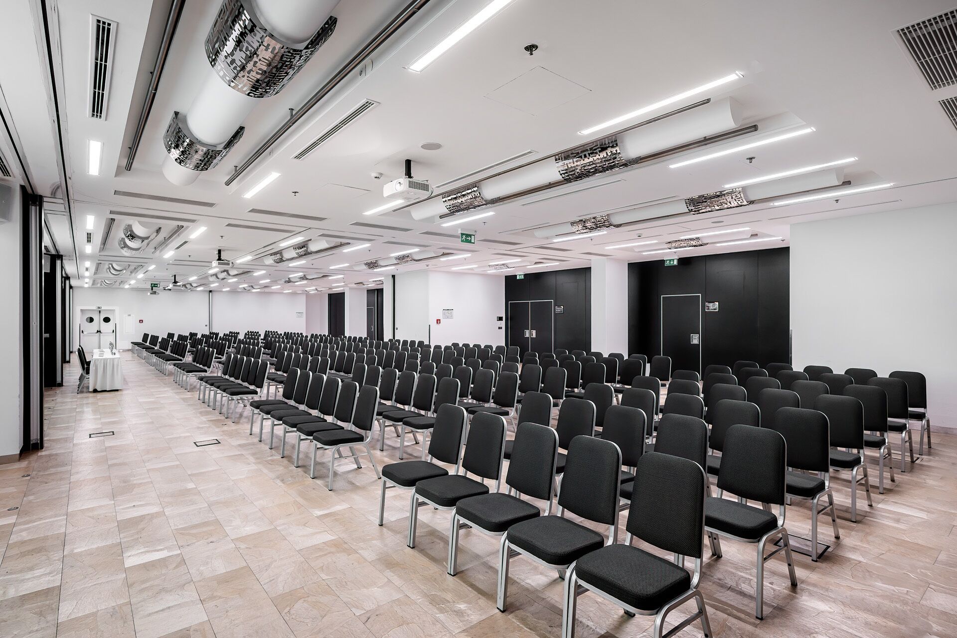 Uma sala de conferências com fileiras de cadeiras, um palco e uma grande porta preta.