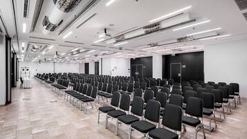 Uma sala de conferências com fileiras de cadeiras, um palco e uma grande porta preta.