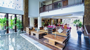 Um hall amplo com teto alto, varanda e área de estar com mobiliário de madeira e plantas em vasos.