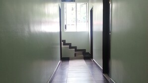 Um corredor com piso ladrilhado, uma escada no final e uma porta à direita.