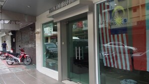 Um HOTEL MAXM com entrada de vidro, uma motocicleta vermelha estacionada do lado de fora e o reflexo de um carro e uma bandeira no vidro.