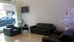 Uma sala de estar com um sofá de couro preto, uma mesa pequena e uma televisão na parede.