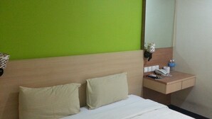 Quarto de hotel com cama, mesa de cabeceira, espelho e parede verde.