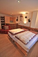Um quarto aconchegante com uma cama de madeira, uma poltrona vermelha e uma área de cozinha ao fundo.