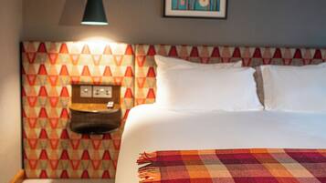 Quarto de hotel com cama, mesa de cabeceira, parede estampada e luminária pendente.