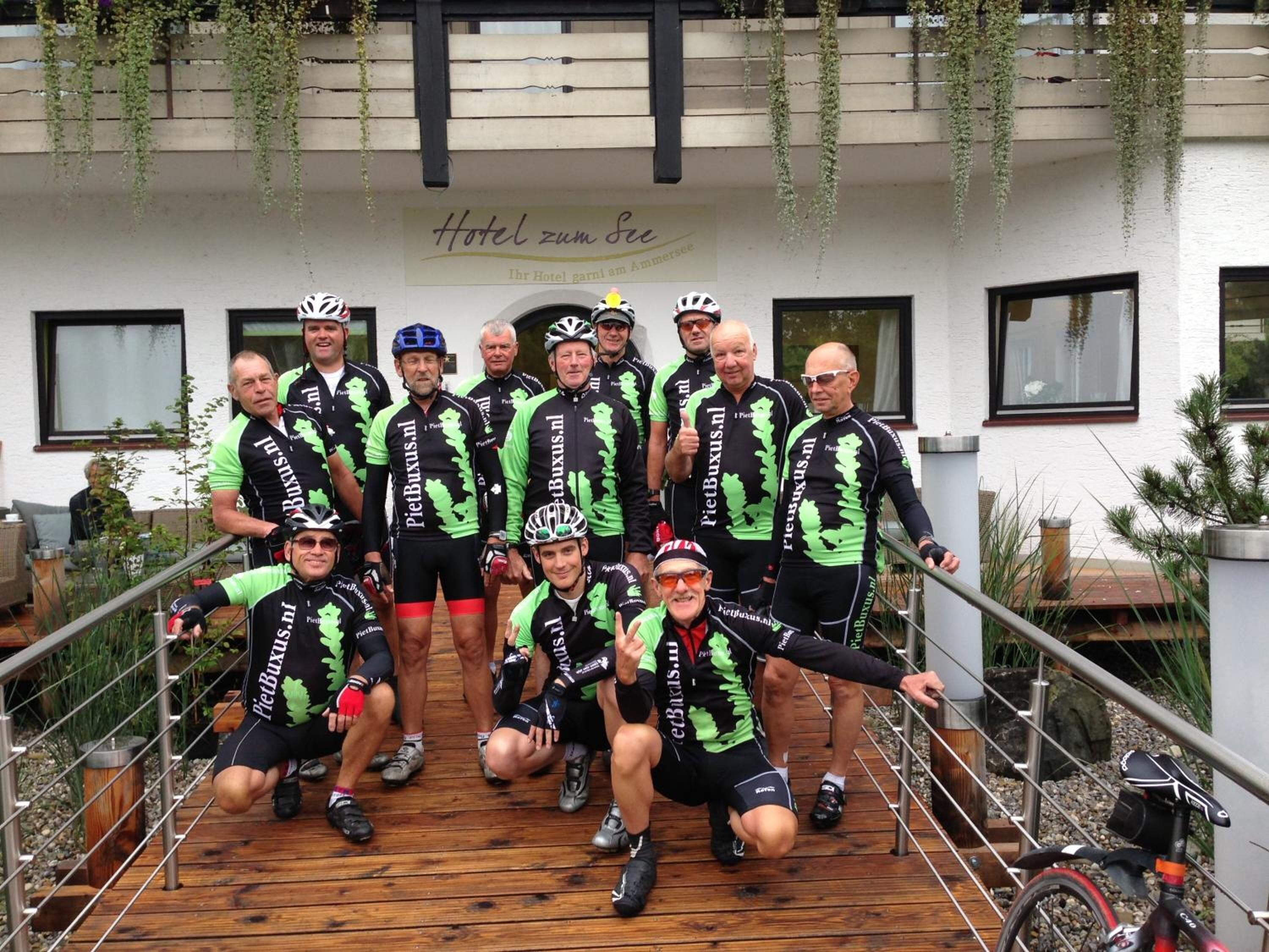 Um grupo de ciclistas posando em frente a um edifício com uma placa que diz 'Hotel zum See'.