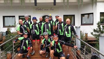 Um grupo de ciclistas posando em frente a um edifício com uma placa que diz 'Hotel zum See'.
