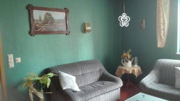 Uma sala de estar com um sofá cinzento, uma mesinha com um vaso e uma cadeira.