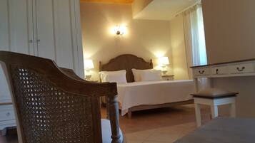 Quarto de hotel com cama de madeira, duas luminárias de cabeceira, mesa de apoio, uma cadeira e uma pequena mesa.