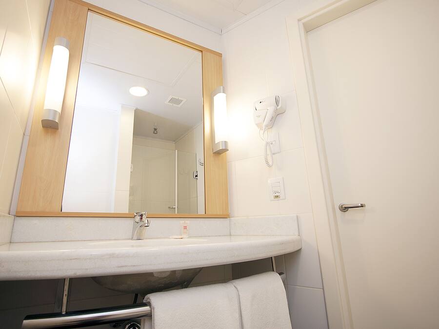 Casa de banho com um espelho grande, lavatório, secador de cabelo e porta-toalhas.