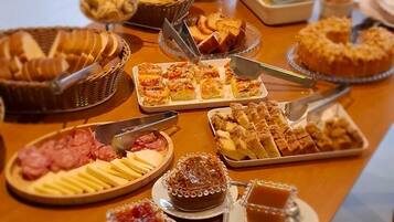 Mesa de buffet com diversos alimentos, incluindo pão, pastelaria, queijo e frutas.