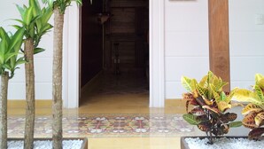 Um arco de madeira que dá entrada a um quarto com piso ladrilhado e uma pequena estátua na parede.