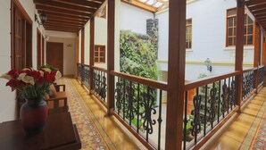 Um corredor com teto de madeira, corrimão com detalhes em ferro forjado e vista para um jardim através do corrimão.