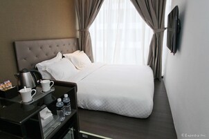 Quarto de hotel com cama, mesa de cabeceira com chaleira, copos e água engarrafada, e uma televisão fixada na parede.