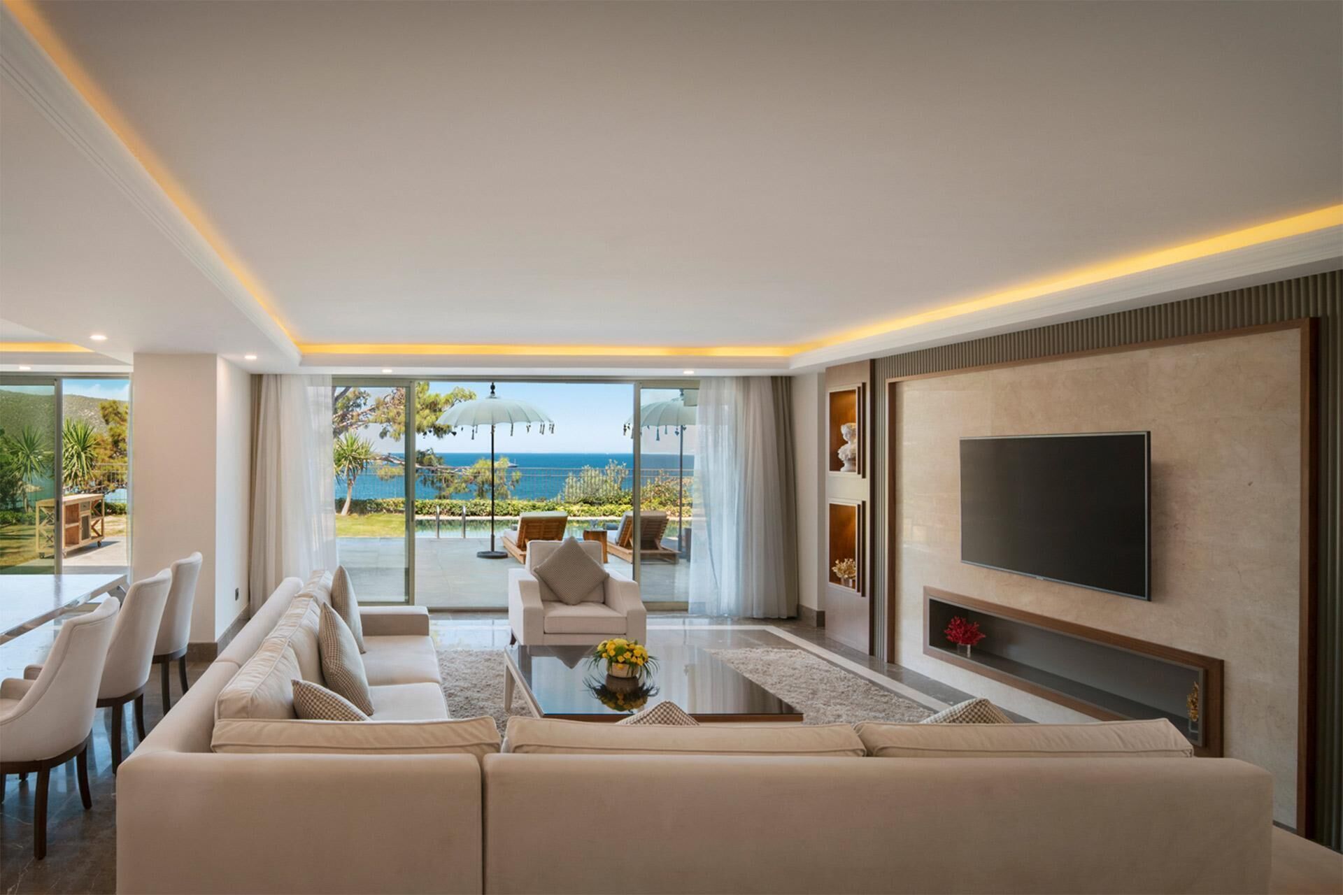 Uma sala de estar moderna com um sofá grande, uma mesa de centro e uma televisão de tela plana na parede.