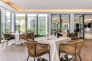 Uma zona de refeições moderna com cadeiras de vime, toalha de mesa branca e divisória de vidro.