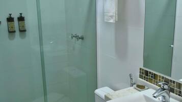 Uma casa de banho com cabine de duche em vidro, sanita, lavatório com espelho e porta-toalhas.