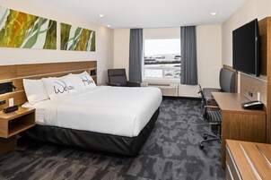 Quarto de hotel com uma cama grande, uma escrivaninha, uma cadeira, uma televisão e obras de arte na parede.
