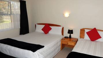 Quarto de hotel com duas camas, uma mesa de cabeceira com abajur, uma janela com cortinas e um candeeiro fixo na parede.