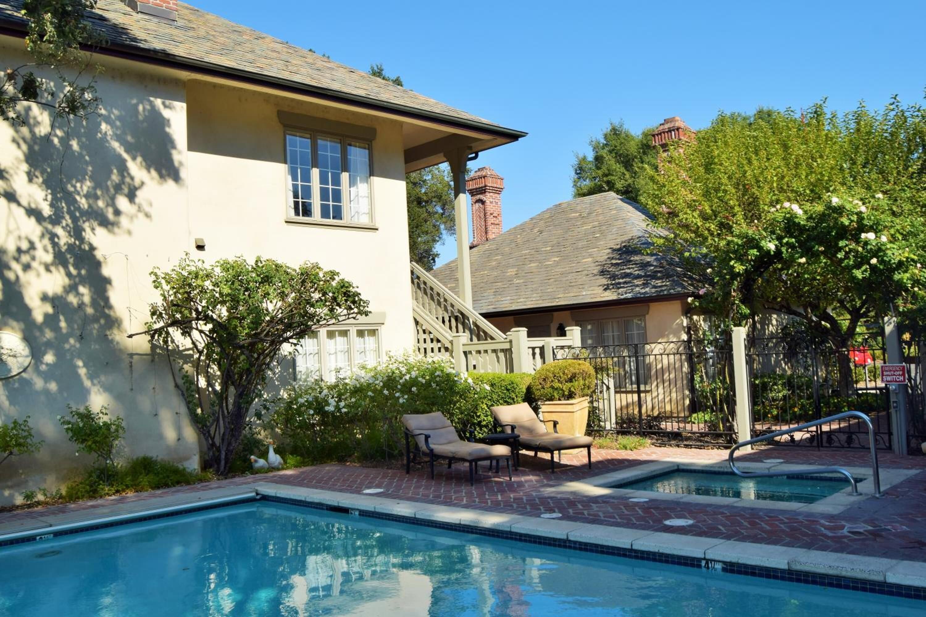 Uma piscina com espreguiçadeiras, um caminho de tijolos e um edifício com chaminé.