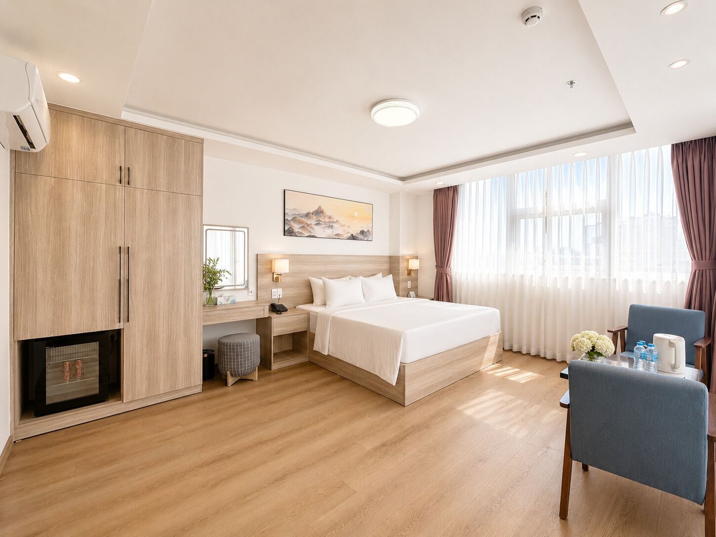 Quarto de hotel com cama, mesa de cabeceira, luminária e vista para o exterior pela janela.