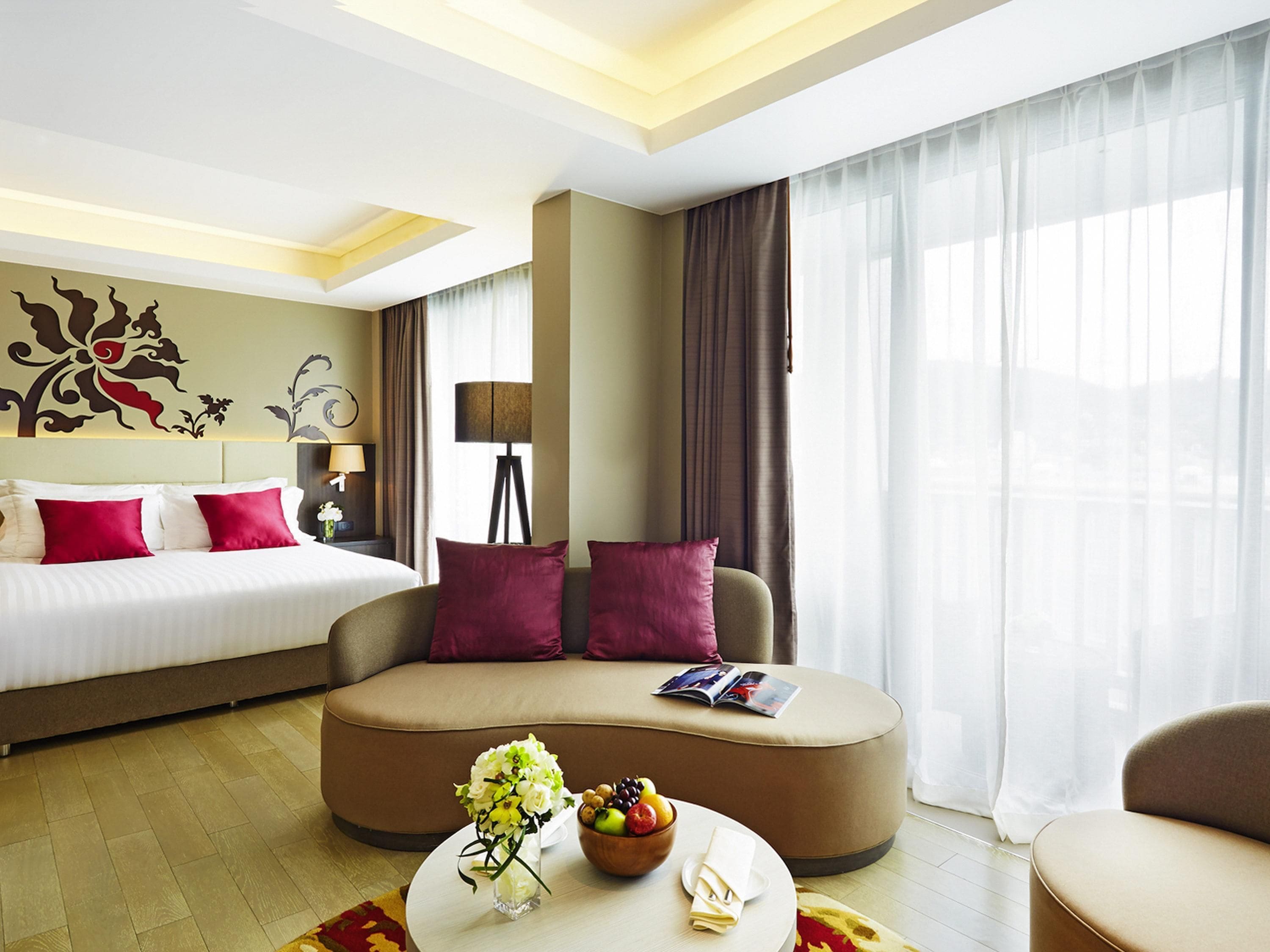 Quarto de hotel com cama, sofá, mesa de centro com frutas e flores, e abajur.