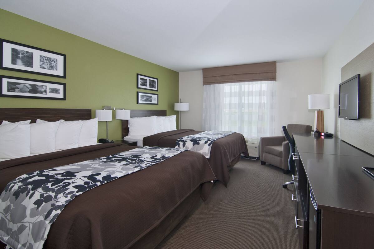 Quarto de hotel com duas camas, uma escrivaninha, uma cadeira e uma televisão.