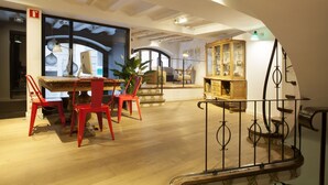Interior moderno com mesa de madeira e cadeiras vermelhas, escada com grades ornamentadas e uma janela grande com vista.