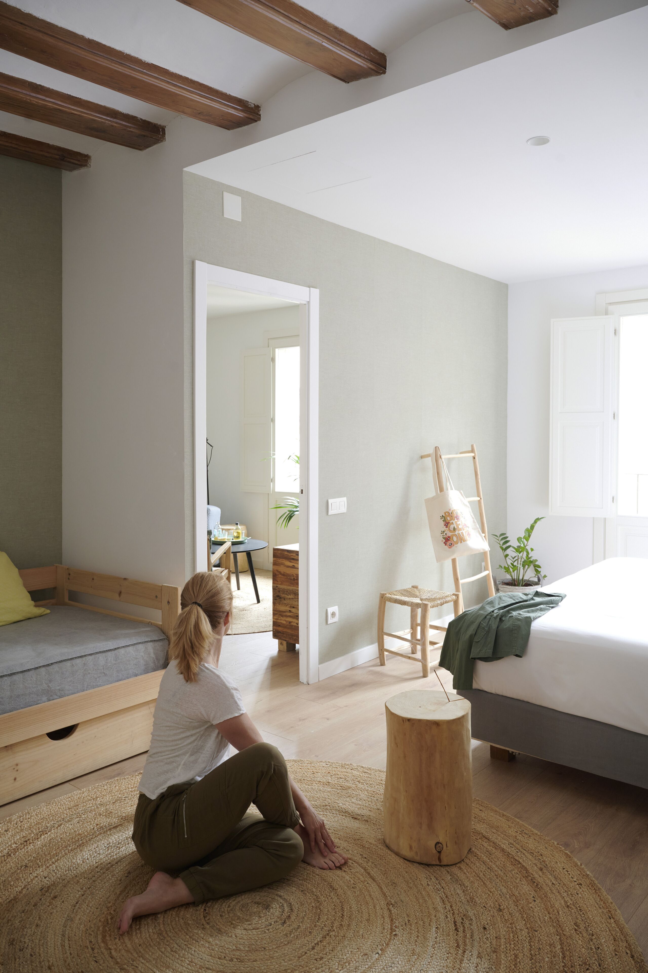 Um quarto com uma cama, uma escada de madeira, um pequeno banco e um vaso com planta.