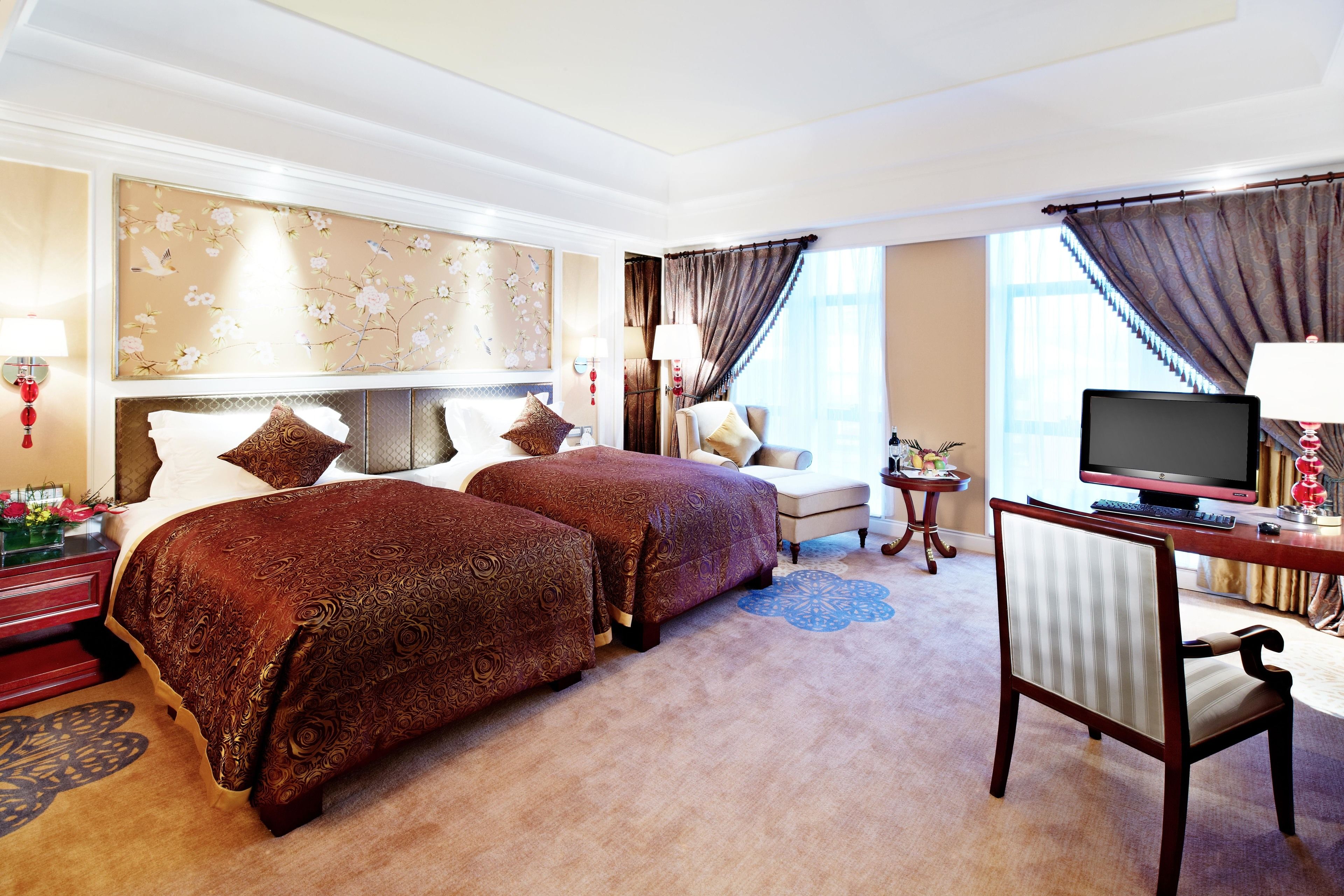 Quarto de hotel com duas camas, uma escrivaninha com computador, uma cadeira e uma televisão.