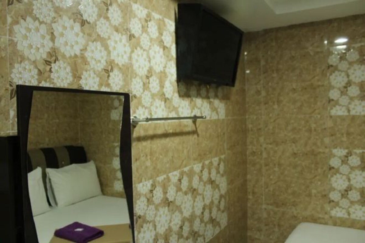 Quarto de hotel com cama, espelho, TV fixada na parede e papel de parede estampado.