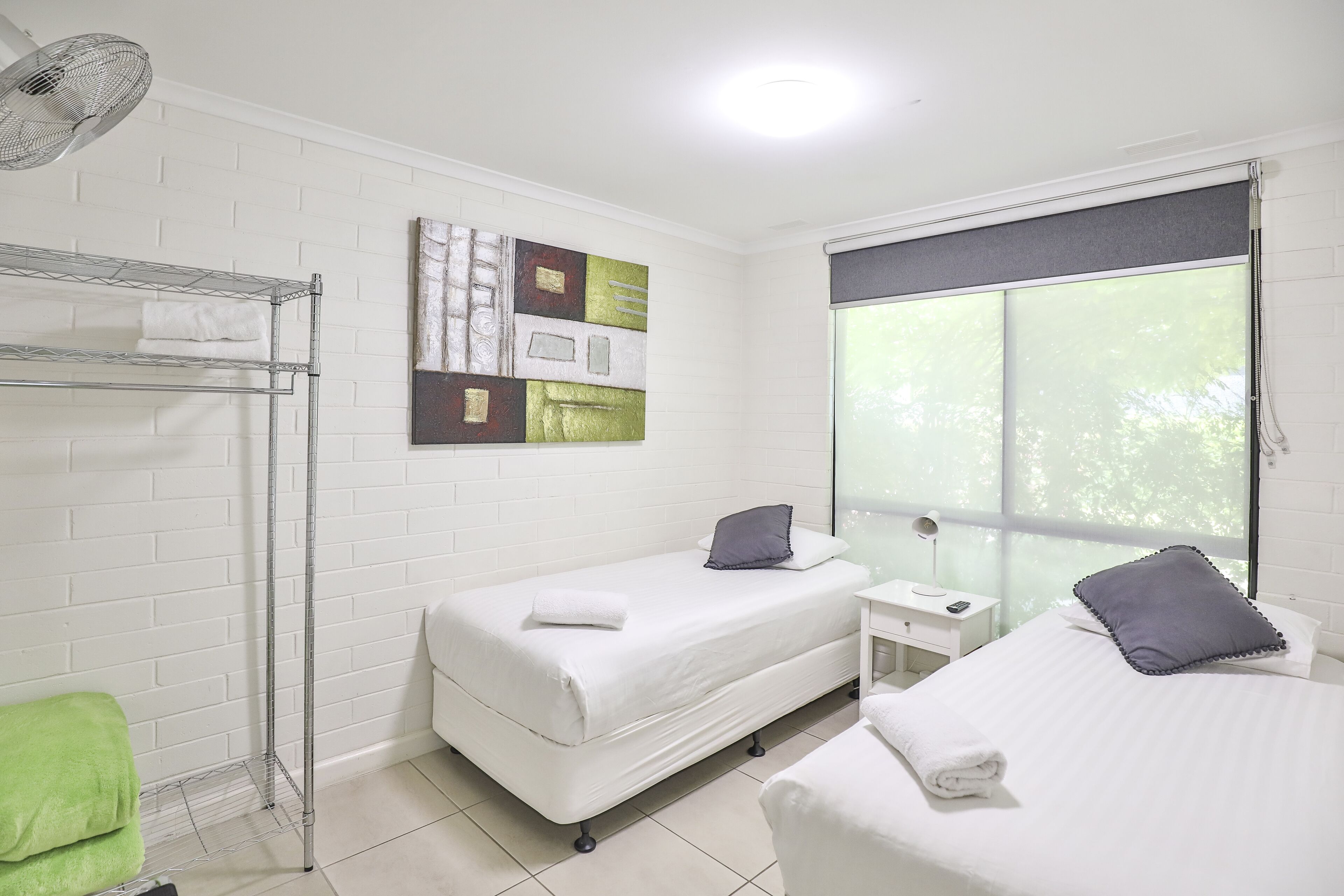 Quarto de hotel com duas camas, janela com vista, obra de arte pendurada na parede e um ventilador.