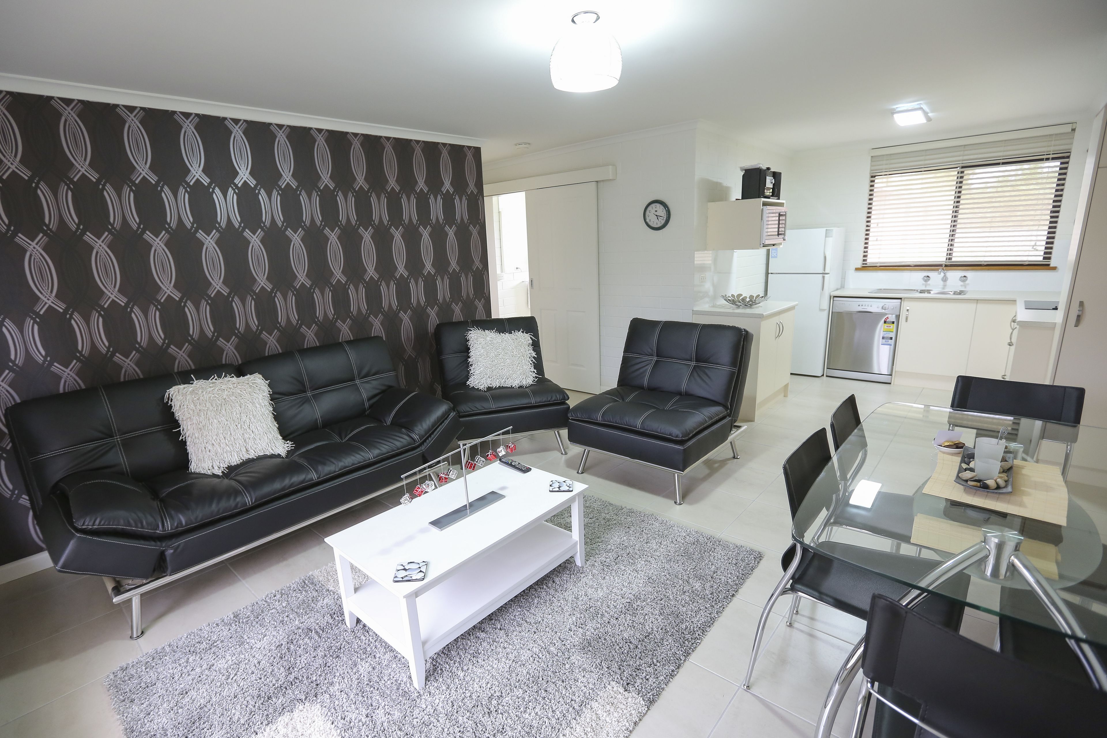 Uma sala de estar moderna com um sofá de couro preto, uma mesa de centro de vidro e uma área de jantar com mesa e cadeiras de vidro.
