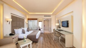 Quarto de hotel com cama, mesa de cabeceira, luminária, televisão e escrivaninha com cadeira.