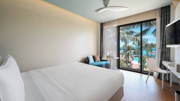 Quarto de hotel com cama, escrivaninha, cadeira e vista para uma piscina e palmeiras.