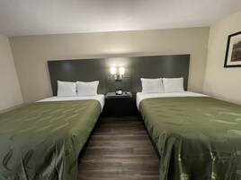 Quarto de hotel com duas camas de solteiro, uma mesa de cabeceira com abajur e uma pequena mesa.