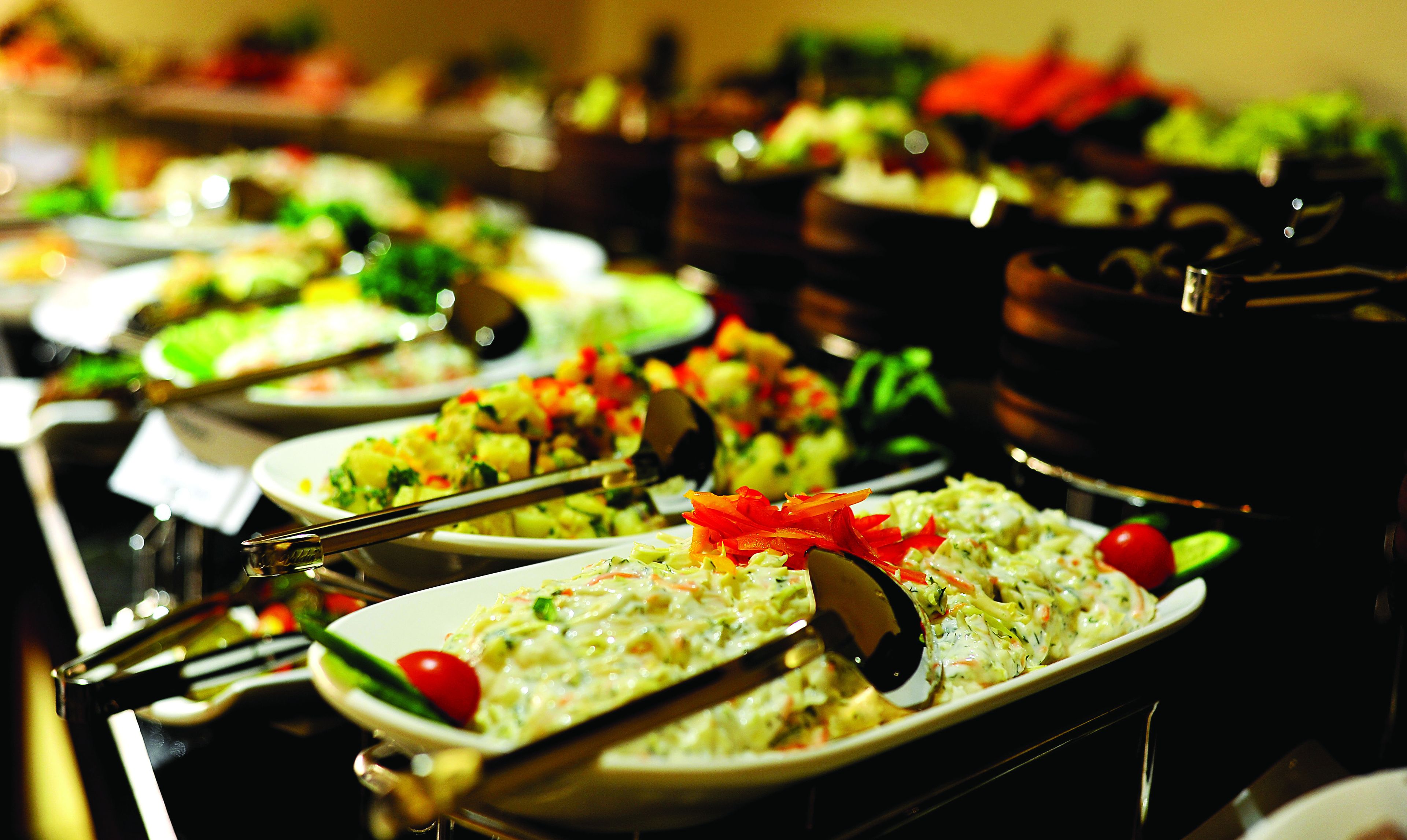 Buffet com diversos pratos, incluindo saladas e um prato de massa, com talheres.