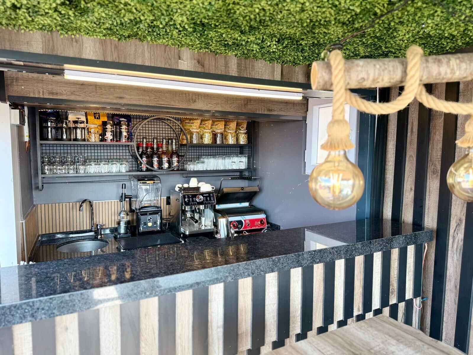 Uma área de bar com uma máquina de café, prateleiras com garrafas e um balcão com padrão listrado.