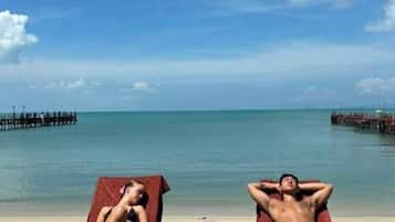 Na praia, areia branca, espreguiçadeiras, guarda-sóis