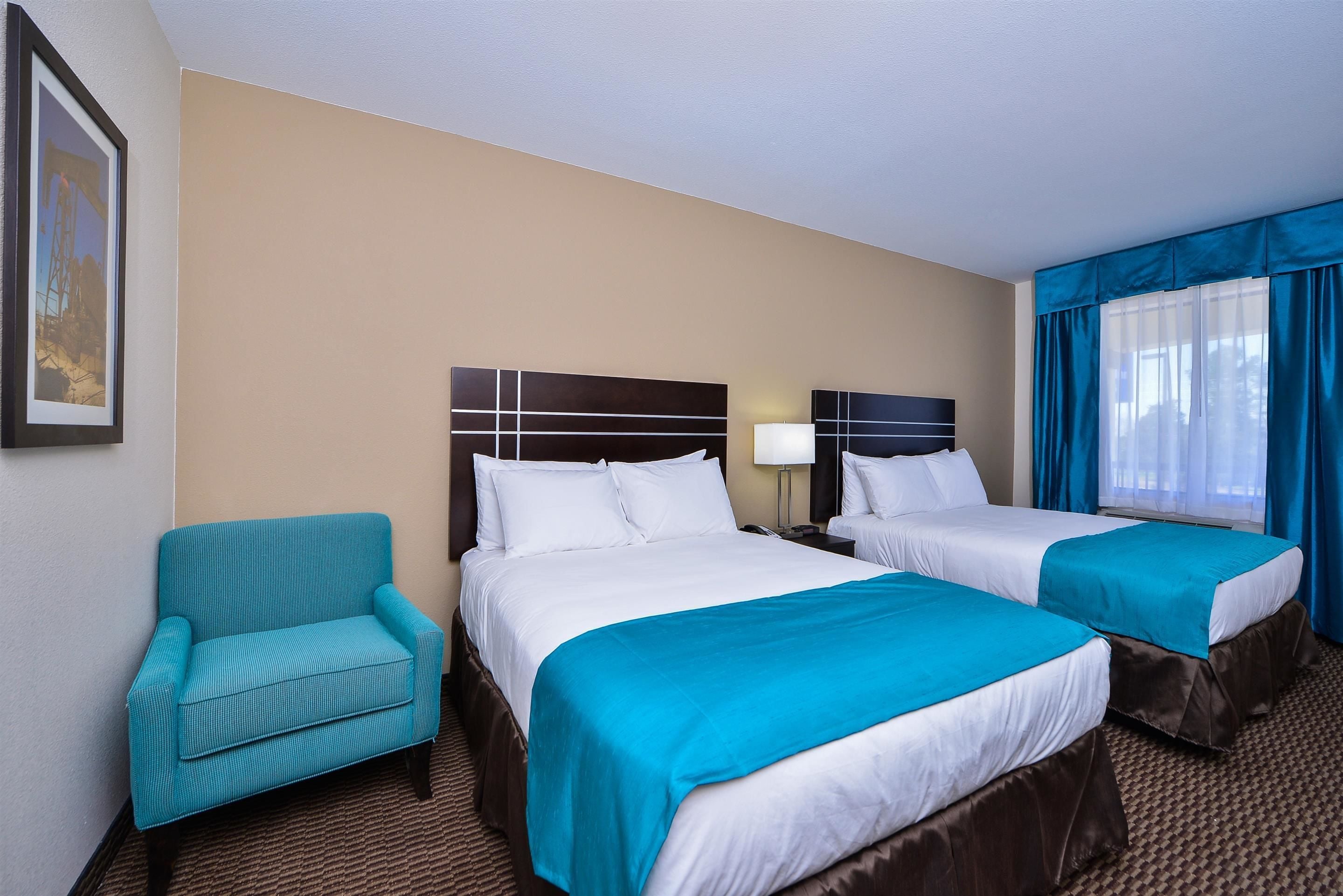 Quarto de hotel com duas camas, uma cadeira e um quadro na parede.