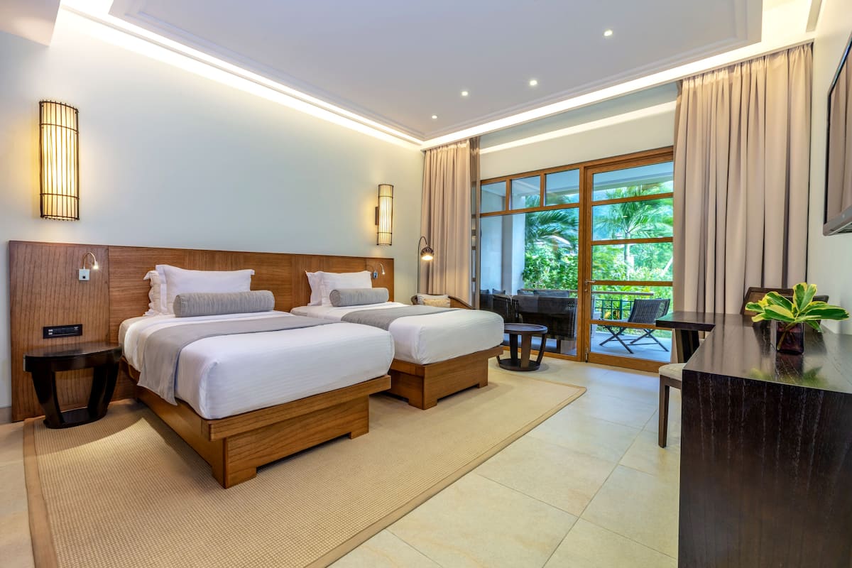 Quarto de hotel com duas camas, uma escrivaninha, uma cadeira e vista para o exterior.