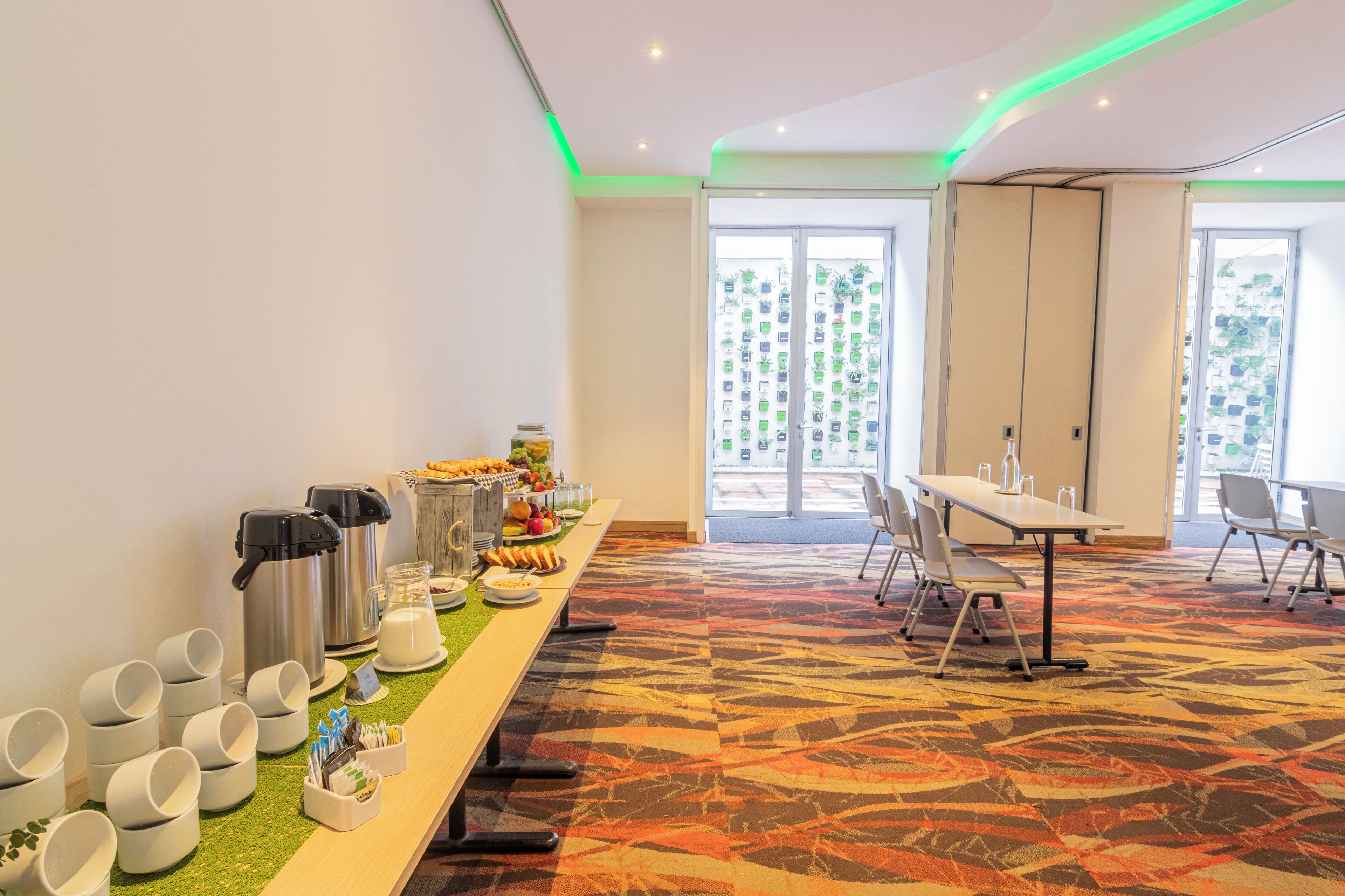 Sala de conferências com uma mesa comprida, cadeiras, um buffet de comida e bebidas, e vista para o verde lá fora.