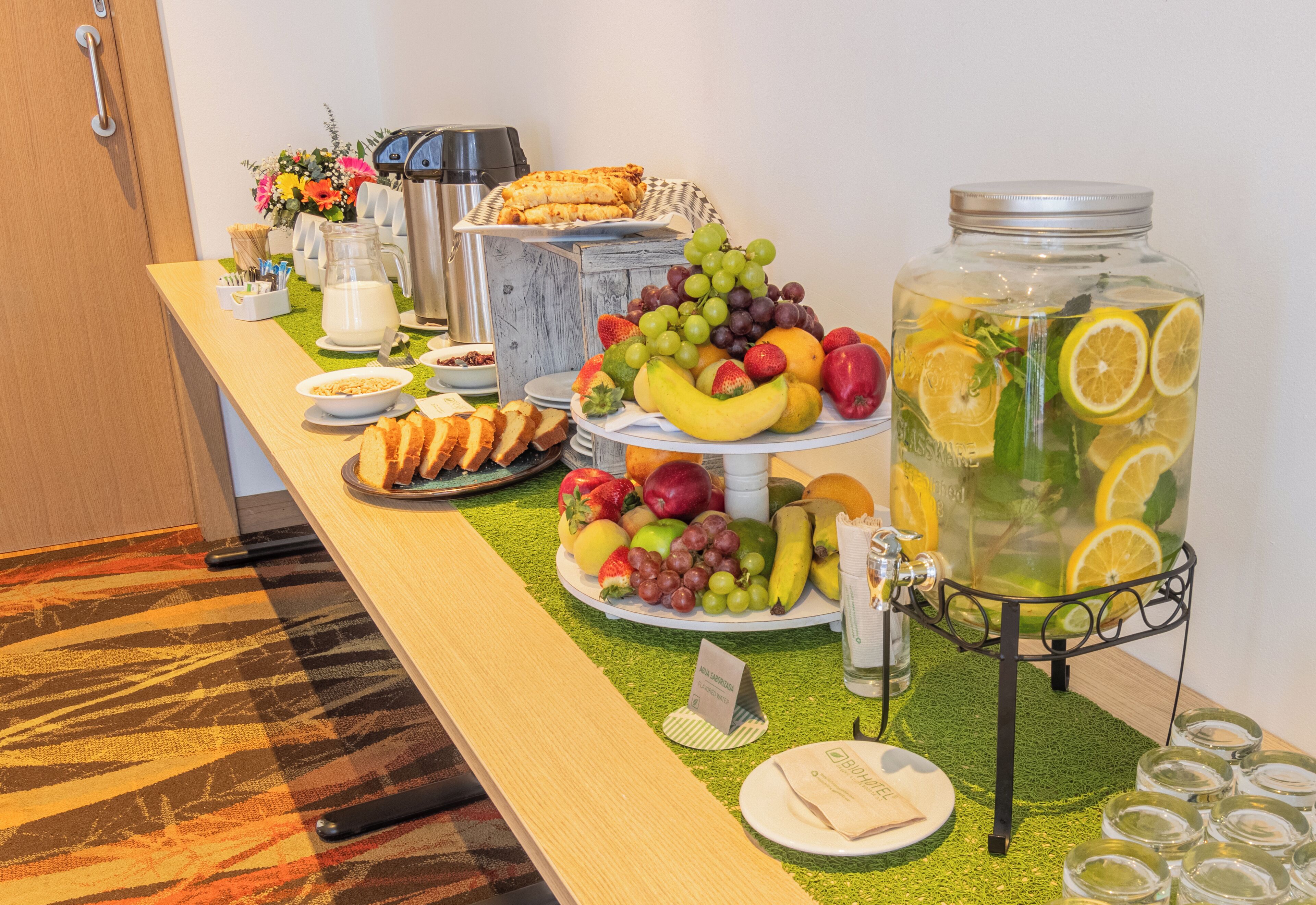 Uma mesa de buffet com diversos alimentos e um grande dispensador de ponche de frutas.