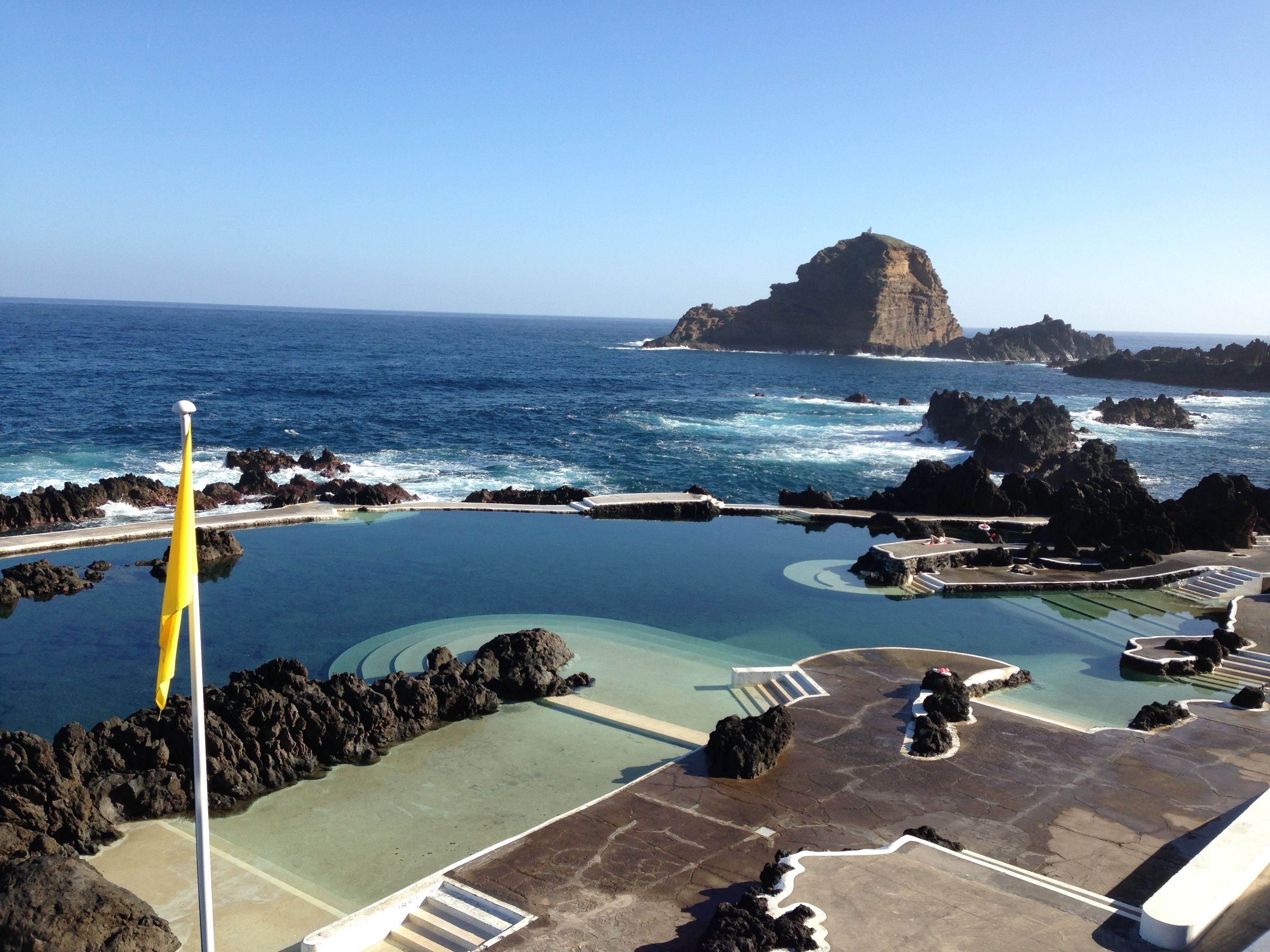 Um resort costeiro com piscina cristalina, litoral rochoso e um mastro.