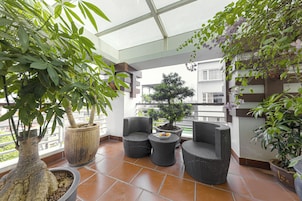 Uma varanda com mobiliário de vime, plantas em vasos e vista para a cidade.
