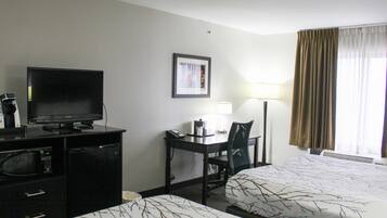 Quarto de hotel com duas camas, uma escrivaninha com cadeira, televisão e luminária.