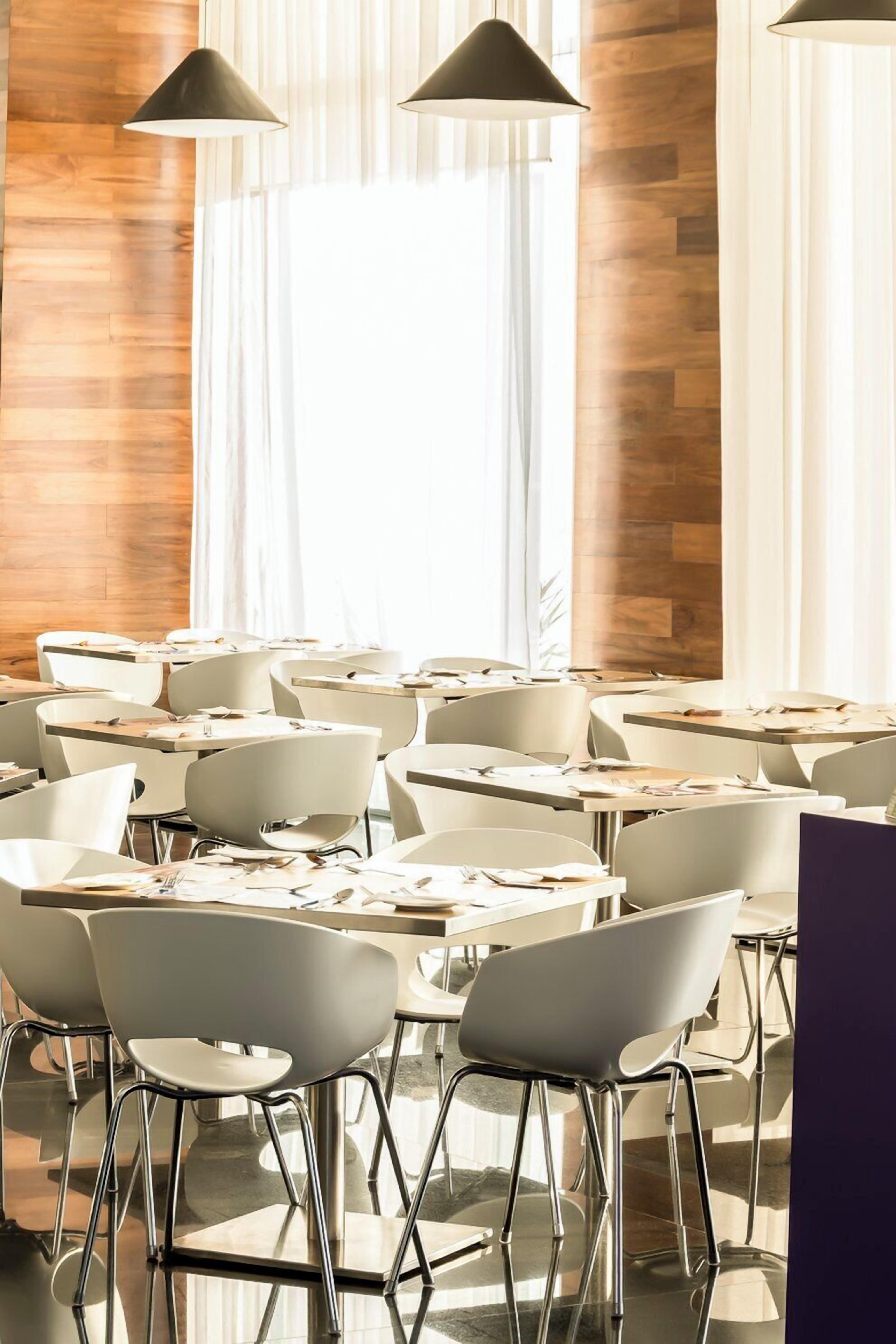 Uma sala de jantar moderna com mesas e cadeiras, painéis de madeira nas paredes e iluminação pendente.